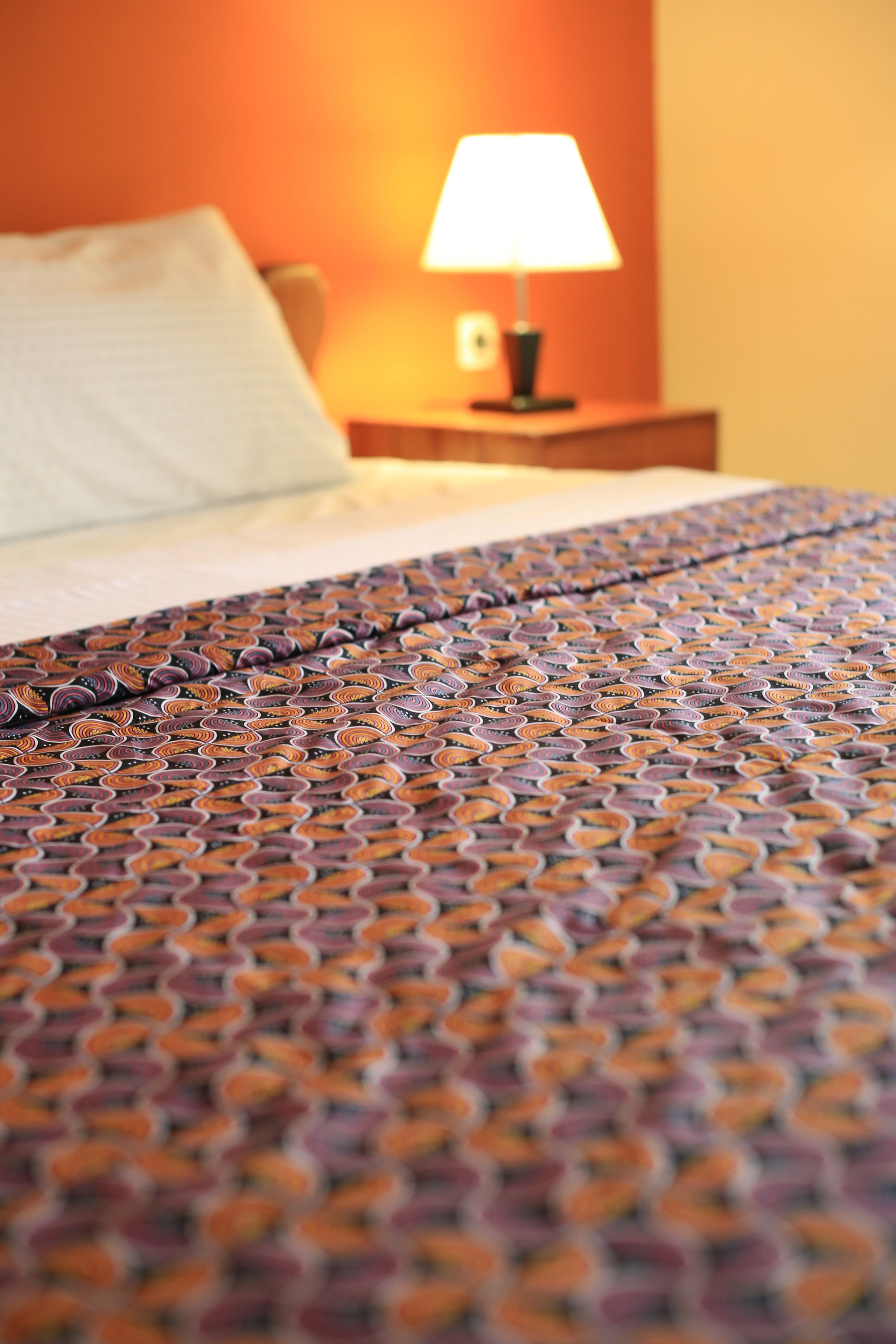 Uma cama com manta estampada, travesseiro e abajur.