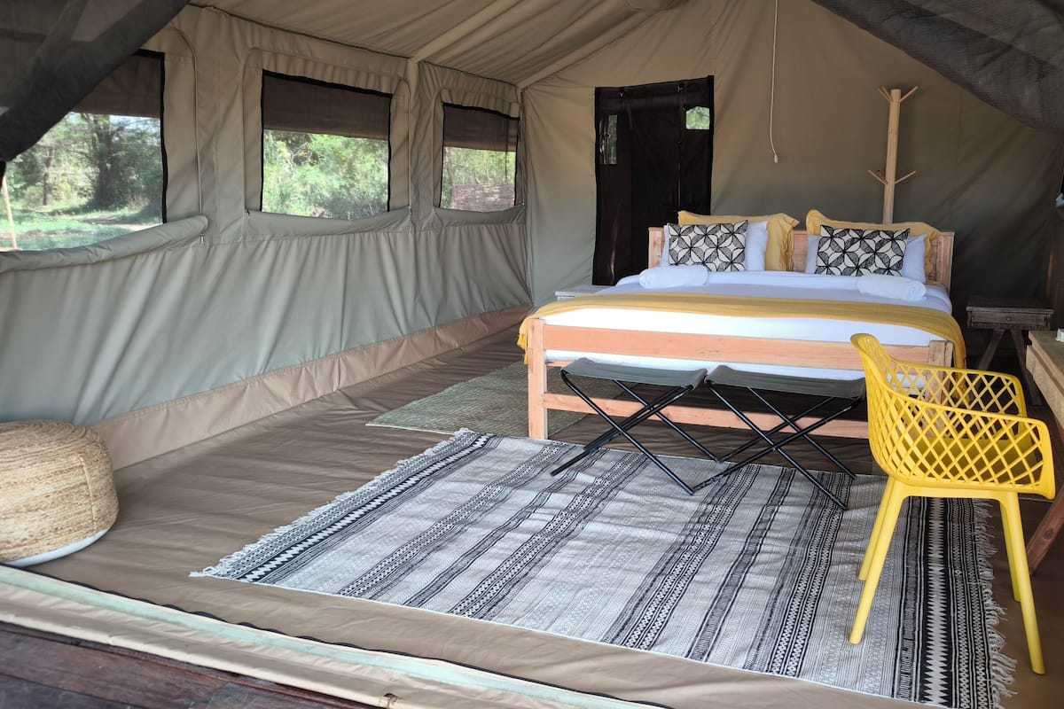 Acomodação em tenda com cama, uma mesinha, uma cadeira e janela.