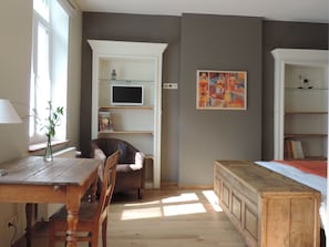 Quarto com mesa de jantar de madeira, uma cadeira, um banco, TV em uma prateleira e um quadro na parede.