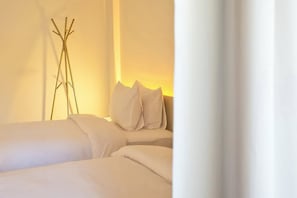 Quarto de hotel com duas camas, uma mesinha de cabeceira e um abajur.