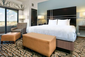 Quarto de hotel com uma cama grande, duas poltronas, uma mesa pequena e vista para o exterior.