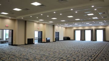 Uma sala de conferências ampla e vazia, com carpete estampado, várias portas e iluminação embutida no teto.