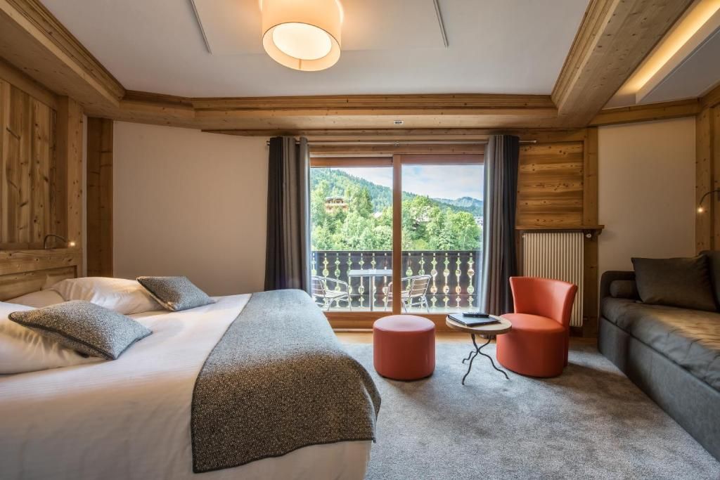 Quarto de hotel com cama, sofá, mesinha e vista para o exterior.