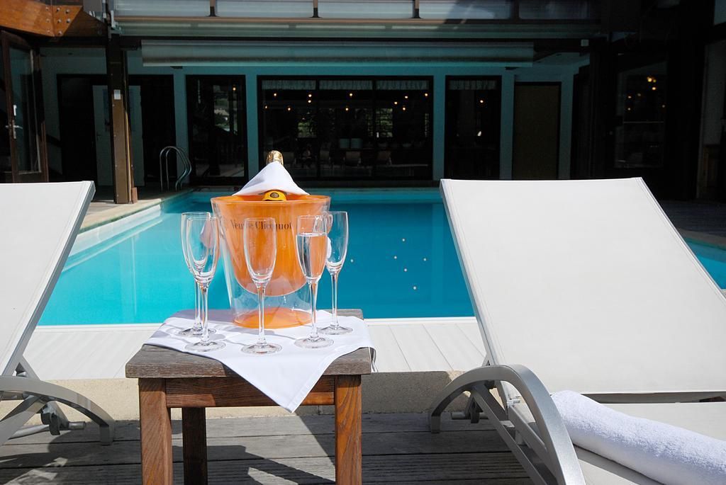 Mesa à beira da piscina com garrafa e copos, uma espreguiçadeira e piscina ao fundo.