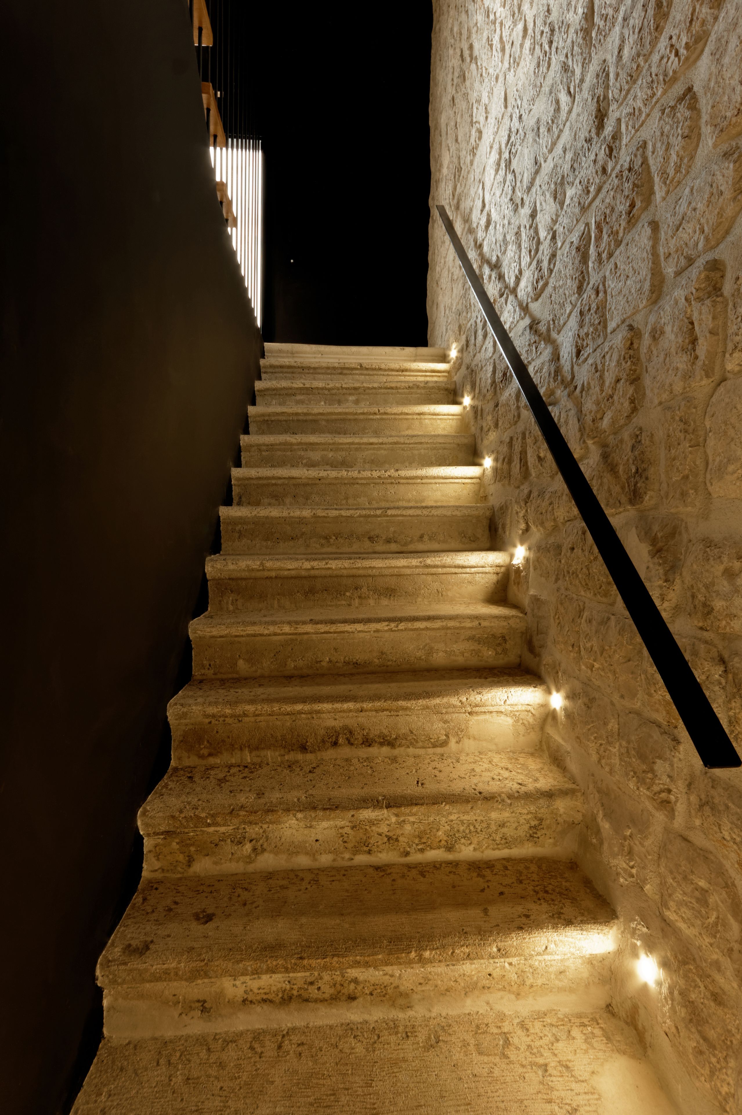 Uma escadaria com paredes de pedra e corrimão, iluminada por pequenas luzes.