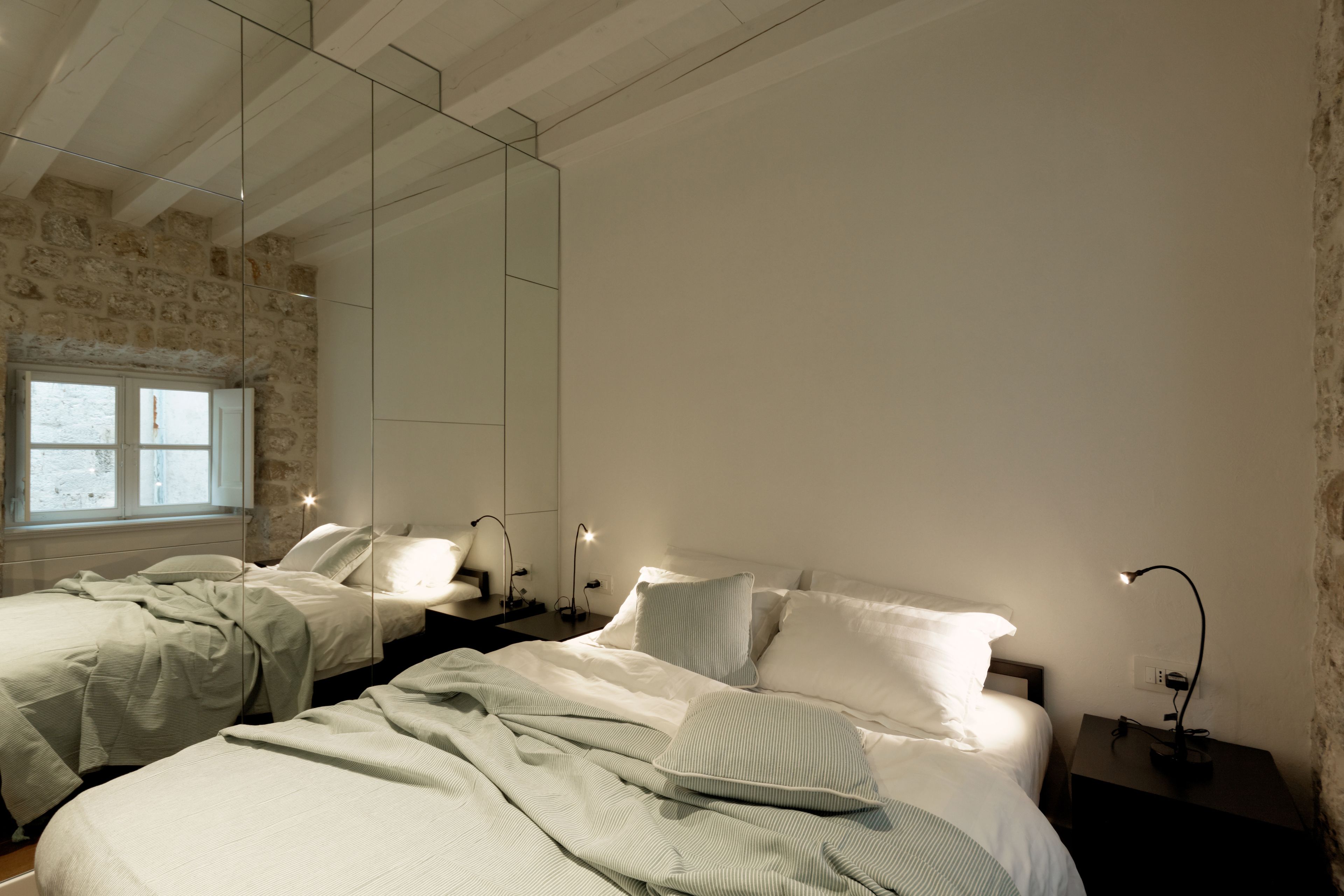 Quarto com duas camas, um espelho grande, abajures e uma parede de pedra.