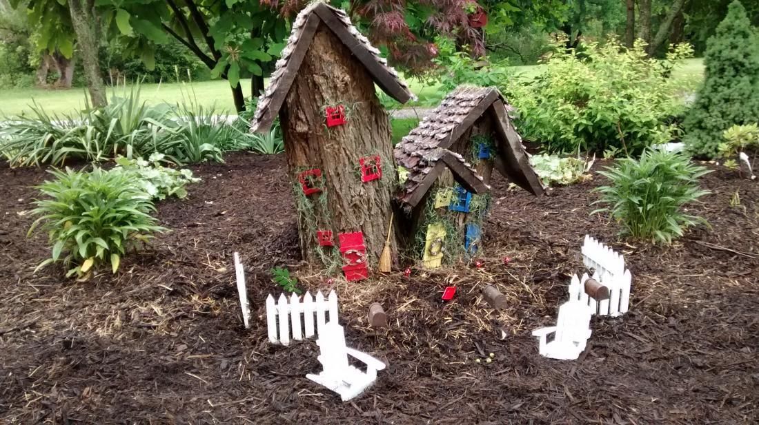 Um jardim com duas casinhas na árvore, cada uma com telhado de palha e cercada por piquetes brancos.