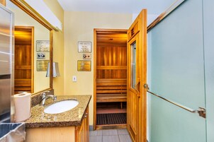 Um banheiro com sauna de madeira, pia com bancada de granito e espelho.