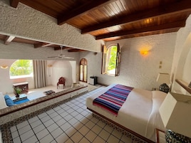 Quarto de hotel com cama, escrivaninha, cadeira e vista para o verde lá fora.