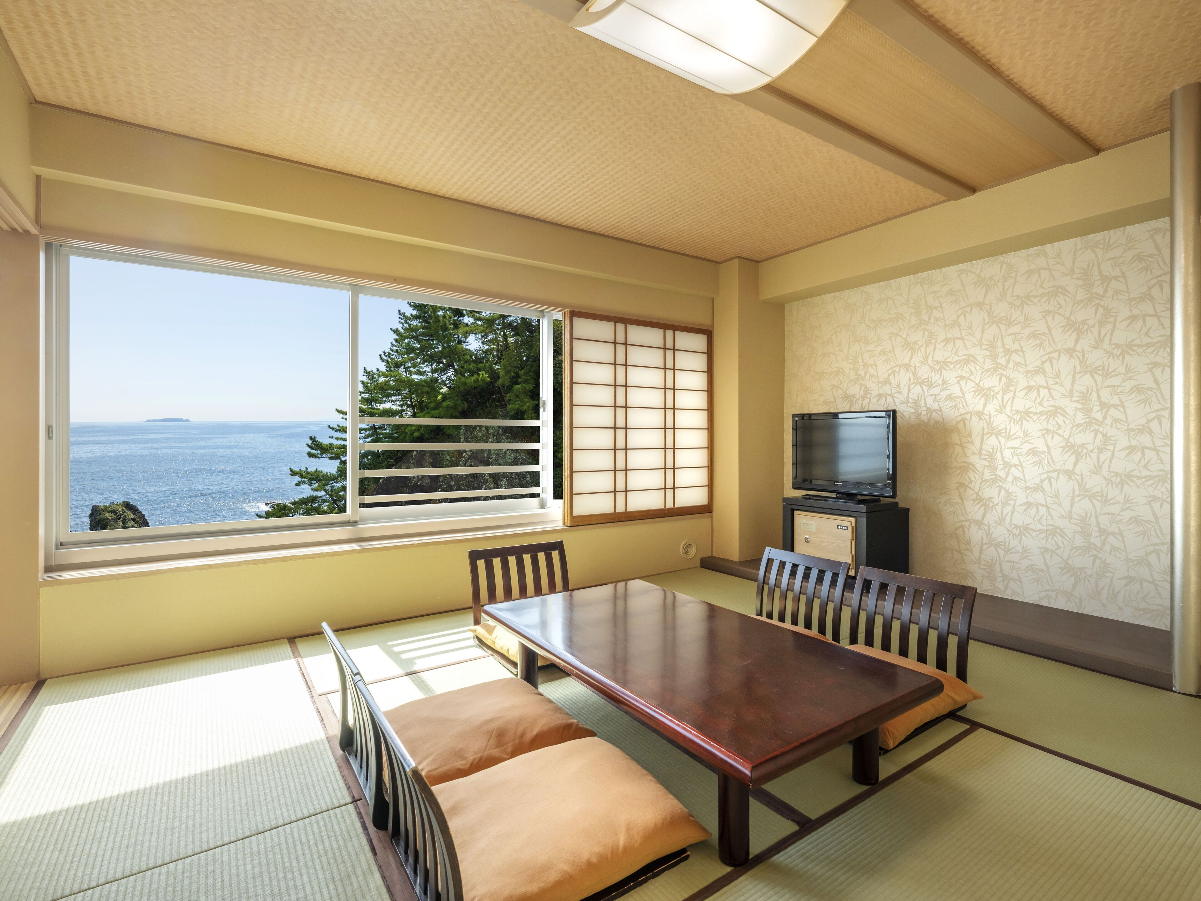 Um quarto japonês tradicional, com tatames, uma mesa baixa com almofadas, televisão e vista para o mar.