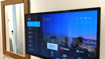 Televisão de tela plana fixada em parede exibindo interface digital com ícones de aplicativos, incluindo Netflix, YouTube e Spotify.