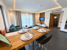 Quarto de hotel moderno com área de jantar, sofá, televisão e vista para o exterior.