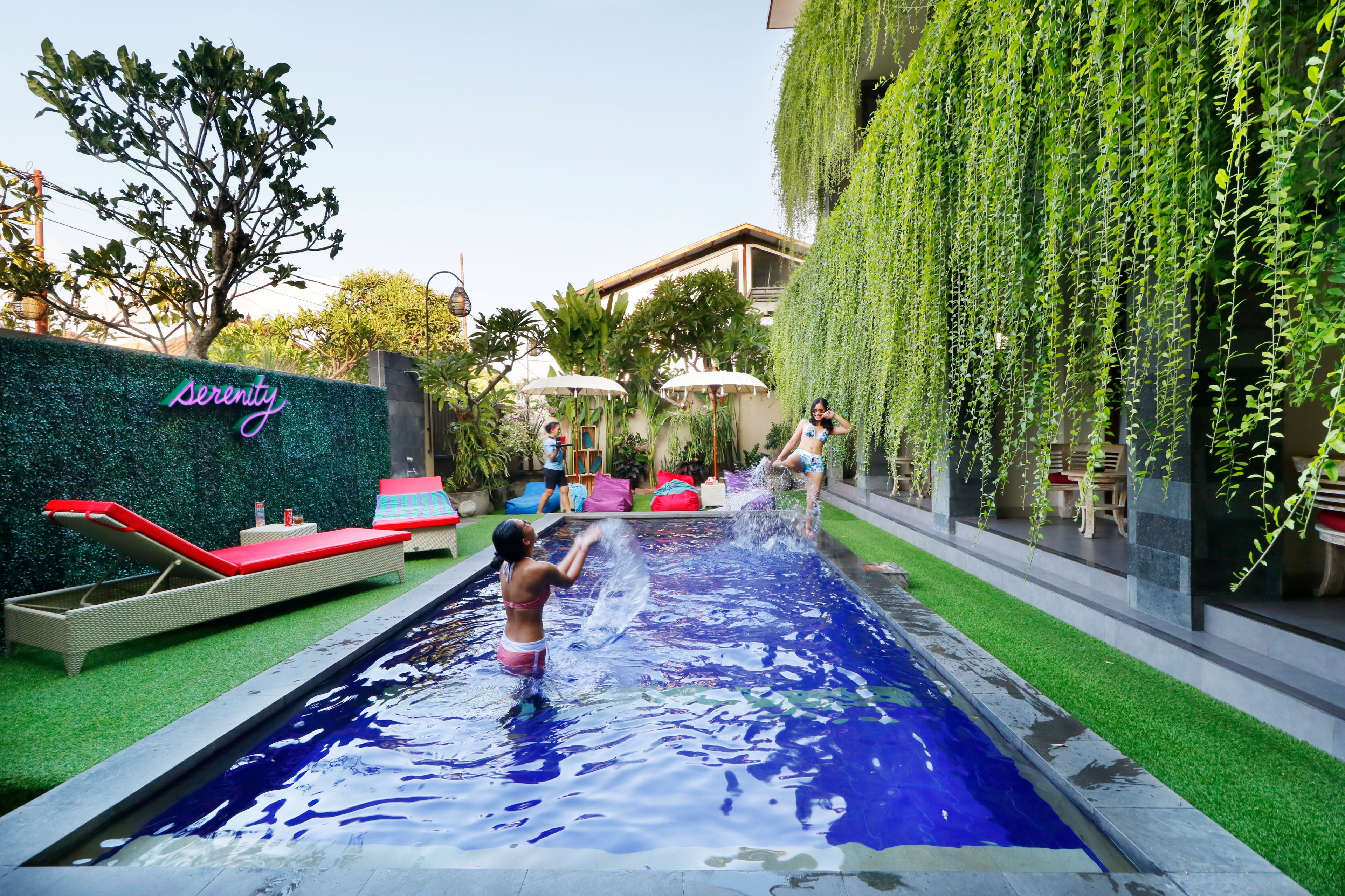 Uma área de piscina com um letreiro 'Serenity', cadeiras de descanso e um espaço de estar coberto.