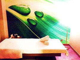 Quarto de hotel com mesa de massagem, toalha e painel de parede com folha e gotas de água.