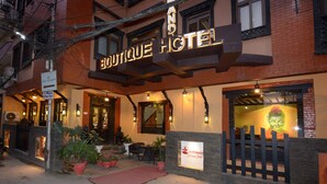 Um hotel boutique com uma placa, plantas em vasos e uma estátua de Buda na entrada.