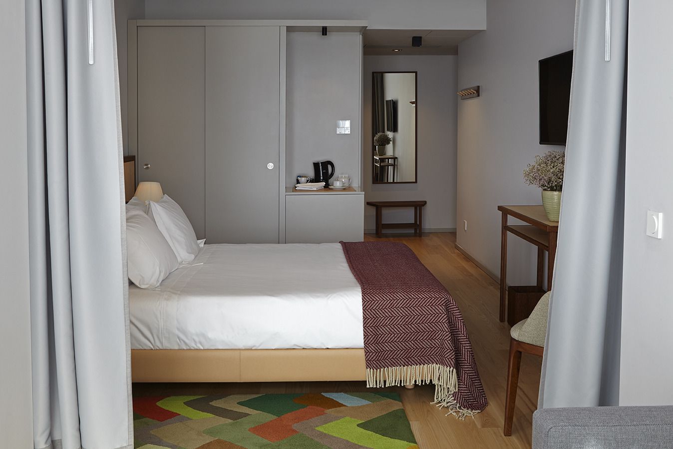 Quarto com cama, mesa de cabeceira, espelho e uma pequena mesa com uma planta.