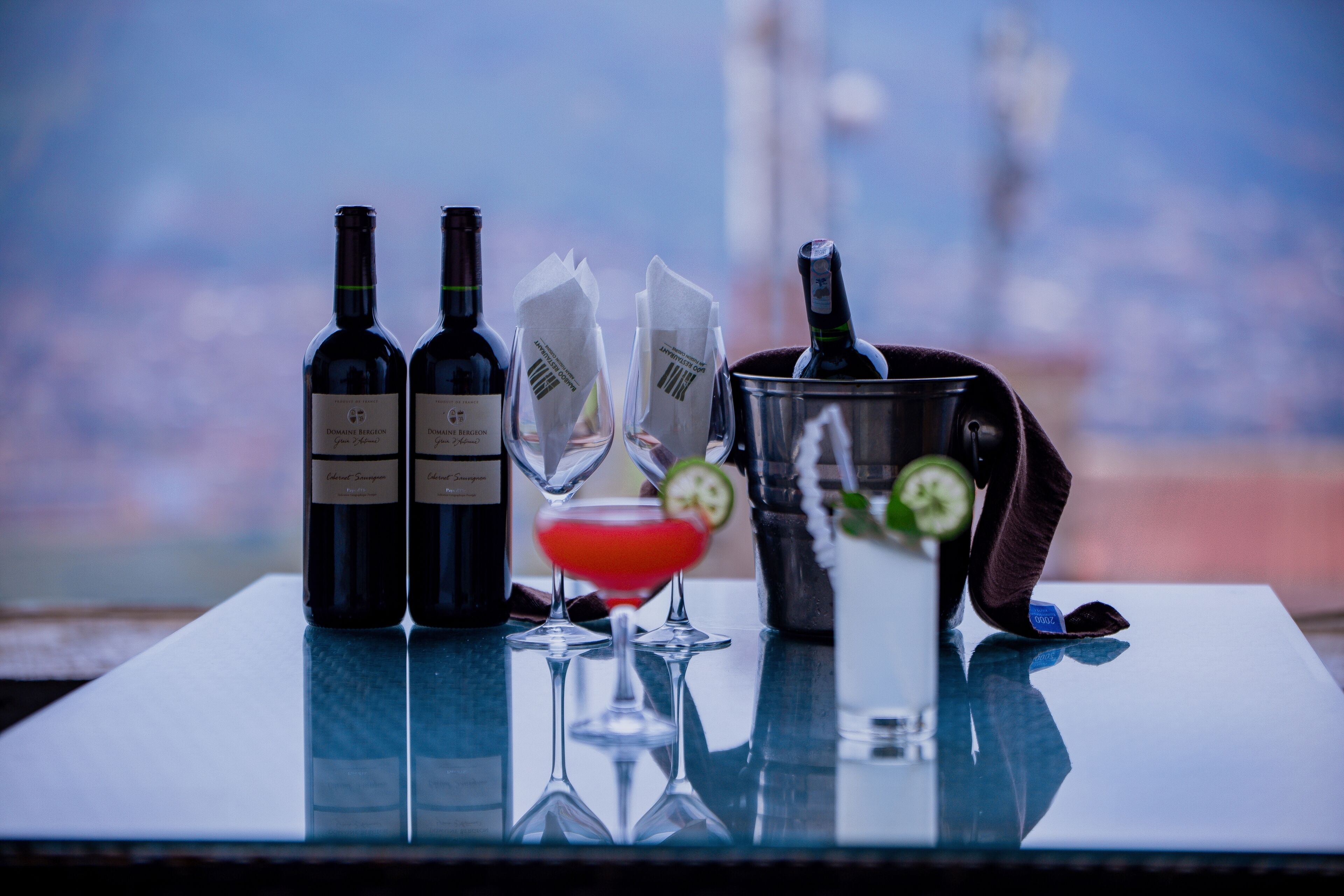 Uma mesa com duas garrafas de vinho, um copo de martini e uma garrafa de champanhe.