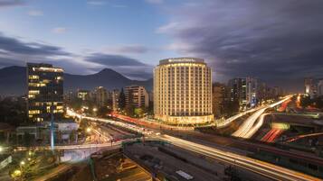 Um hotel com várias andares e uma estrutura circular imponente, situado numa área urbana movimentada com ruas e obras visíveis.