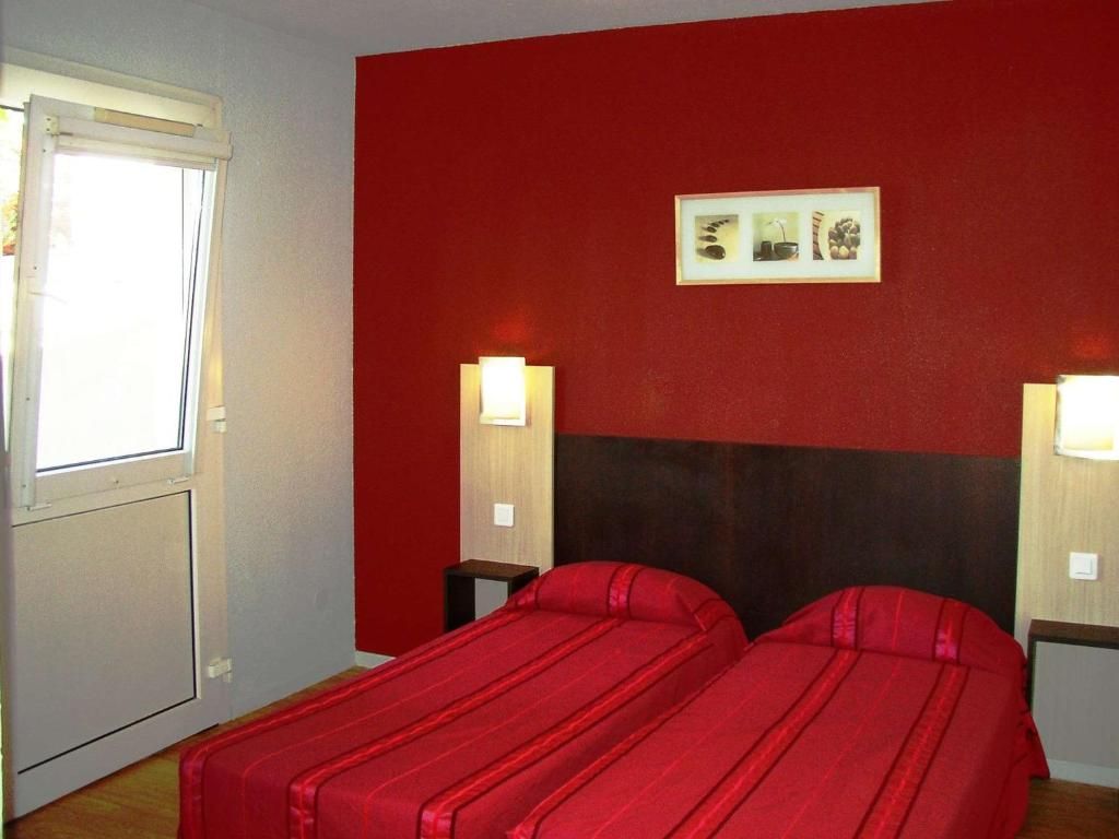 Quarto de hotel com duas camas, parede vermelha, quadro emoldurado e duas luminárias de cabeceira.