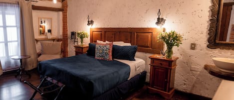 Quarto com cama de madeira, mesa de cabeceira, mesa com um vaso, espelho e piso de madeira.
