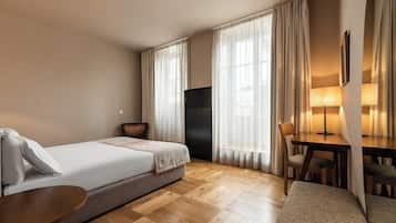 Quarto de hotel com uma cama, uma escrivaninha com cadeira, televisão e luminária.
