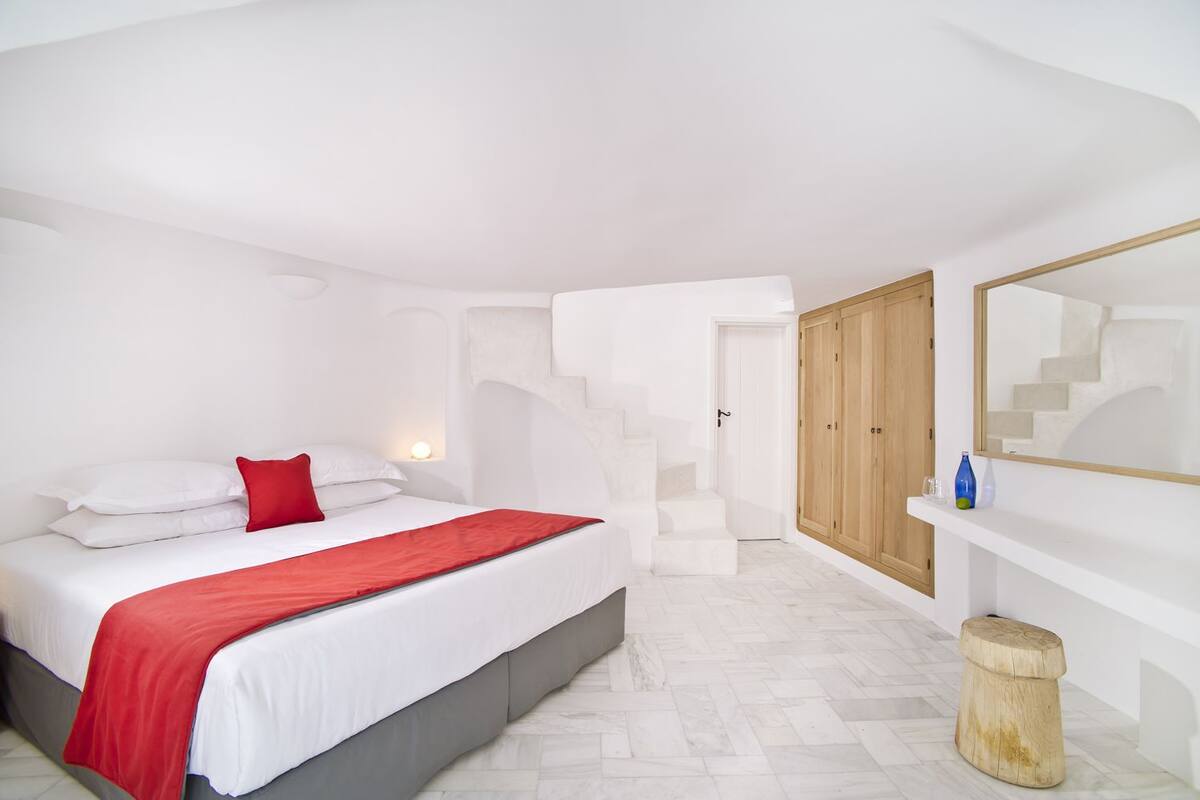 Um quarto com cama, travesseiro vermelho, guarda-roupa de madeira e espelho na parede.