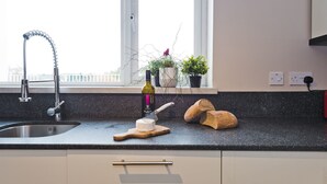 Uma cozinha com pia de aço inoxidável, uma garrafa de vinho, uma faca de queijo e pão na bancada.