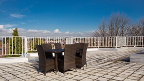 Um pátio externo com mesa e cadeiras, piso de azulejos e cerca branca.