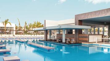 Uma área de piscina moderna de hotel, com várias pistas para natação, espreguiçadeiras e um bar.