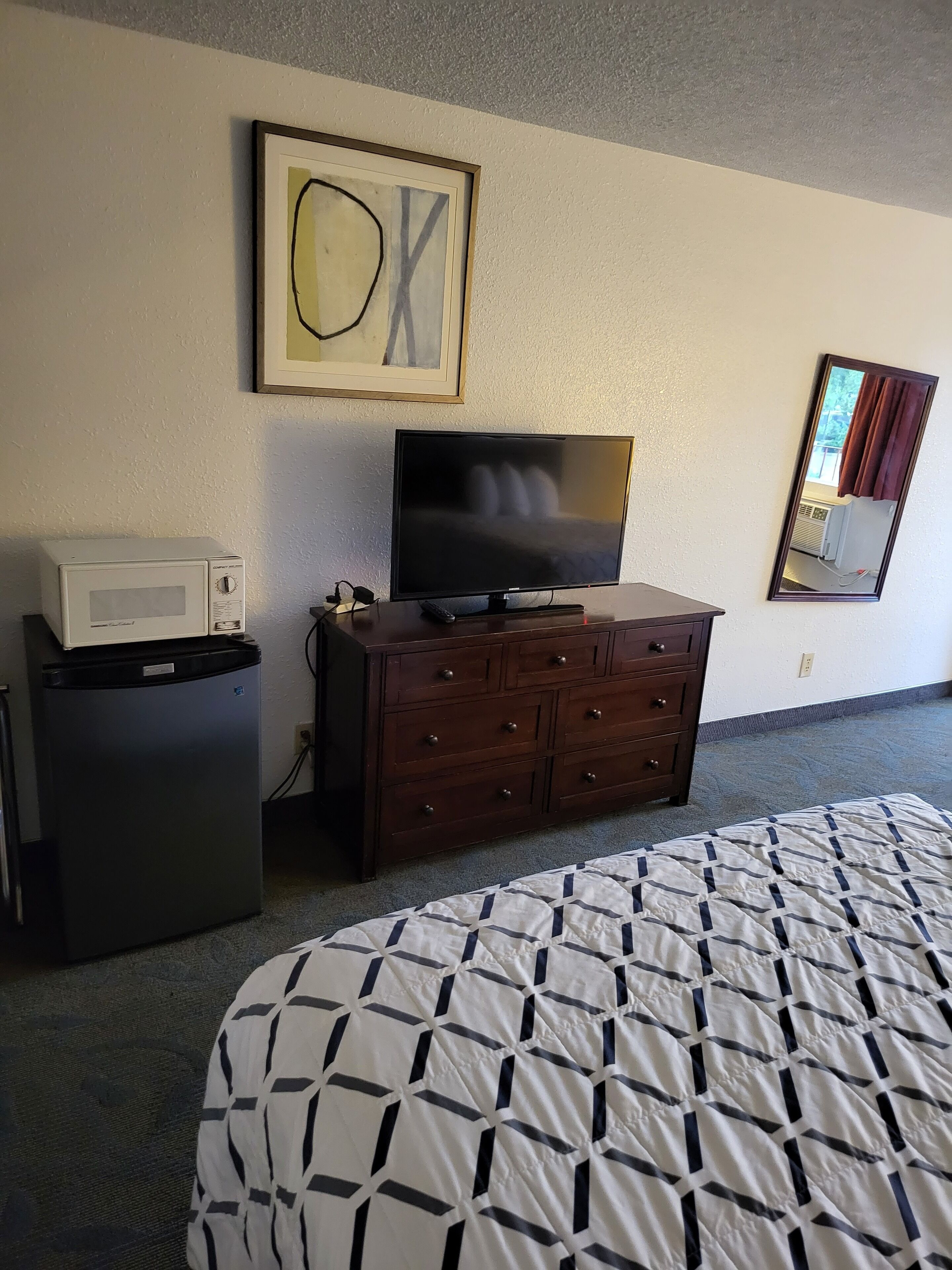 Quarto de hotel com cama, televisão, micro-ondas e cómoda.