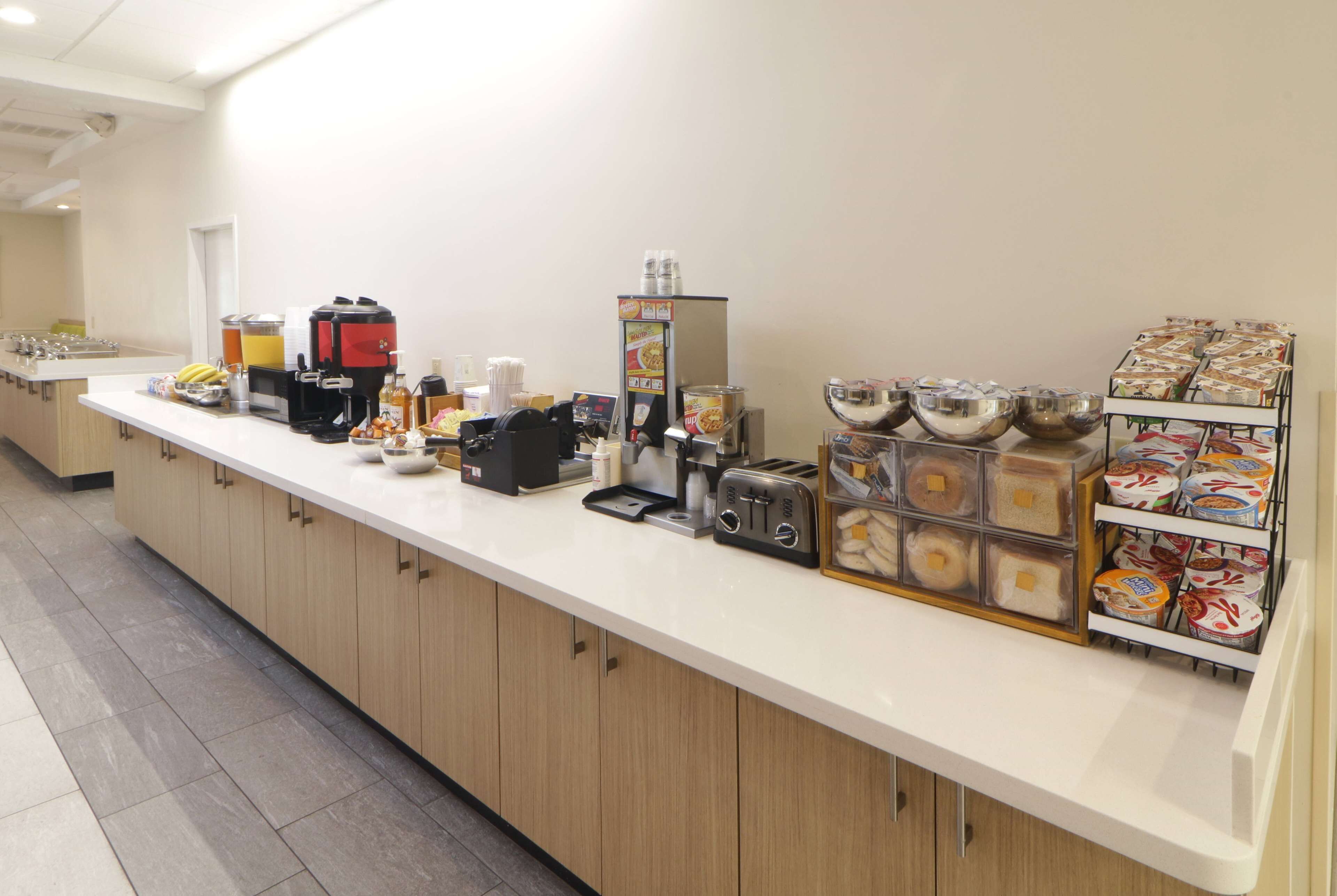 Um balcão de café da manhã com diversos alimentos, uma máquina de café e uma torradeira.