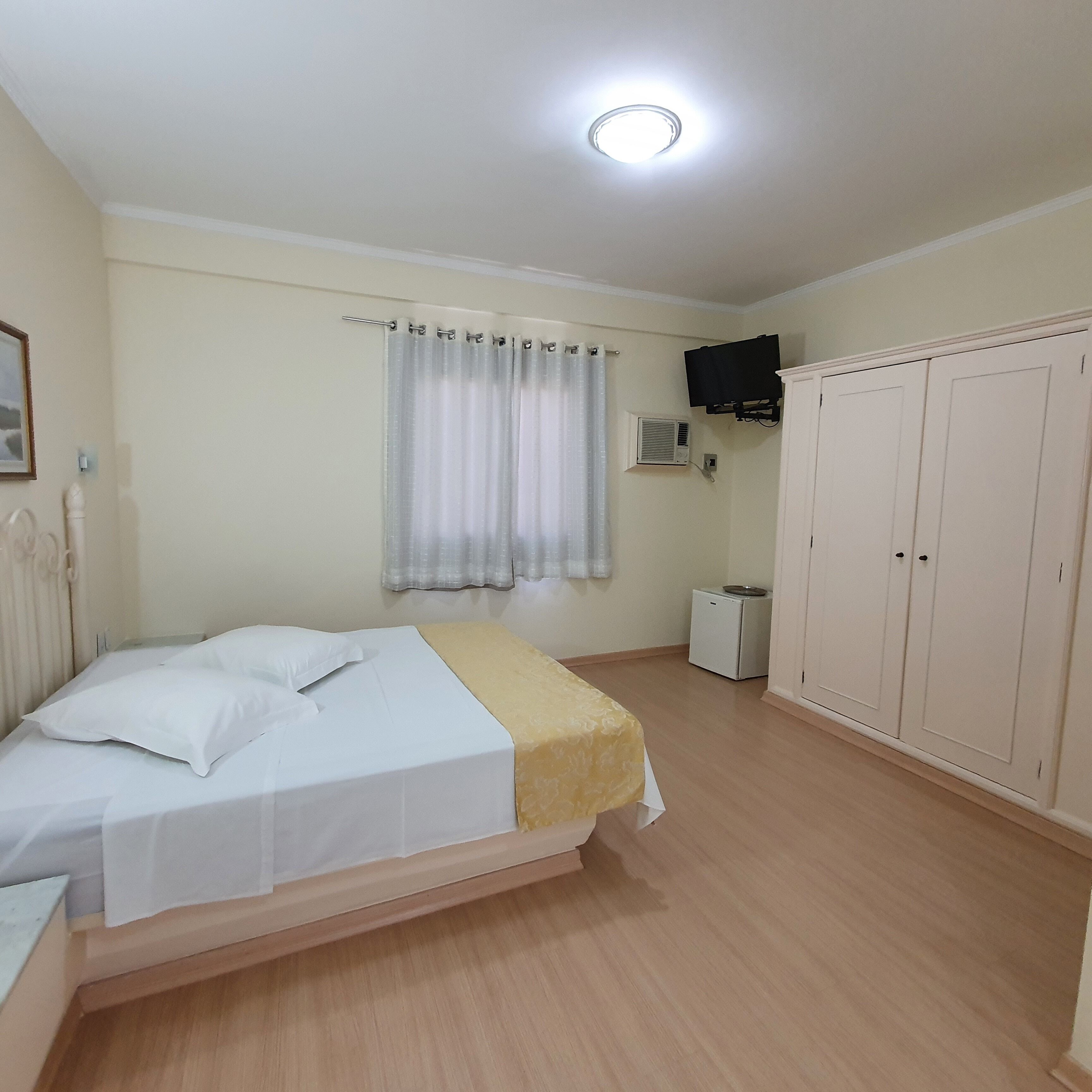 Quarto com cama, guarda-roupa, televisão e ar condicionado.