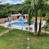 Uma área de piscina com espreguiçadeiras, um pequeno edifício e palmeiras.
