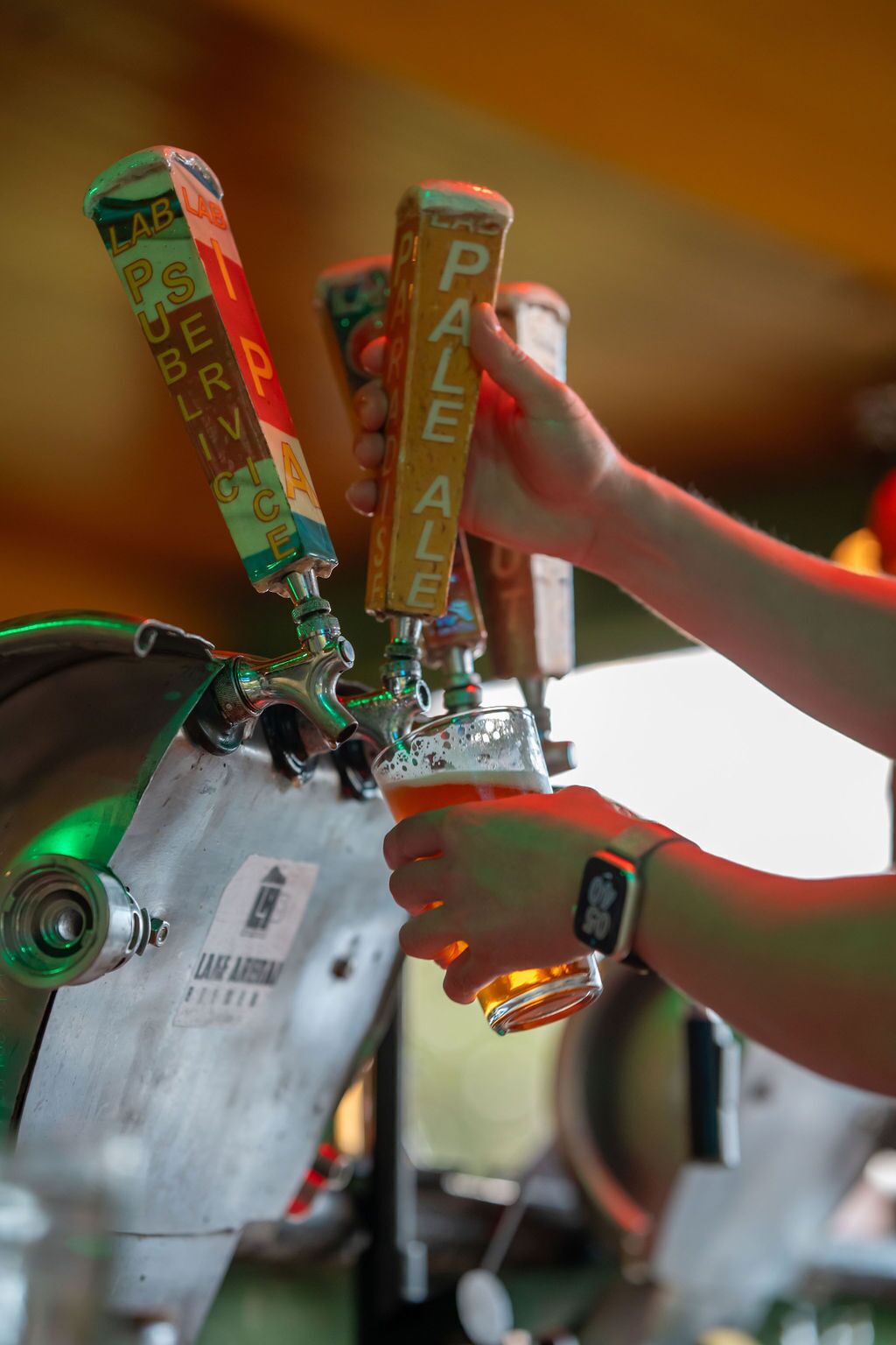 Uma mão servindo cerveja de uma torneira com a etiqueta 'PALE ALE'.