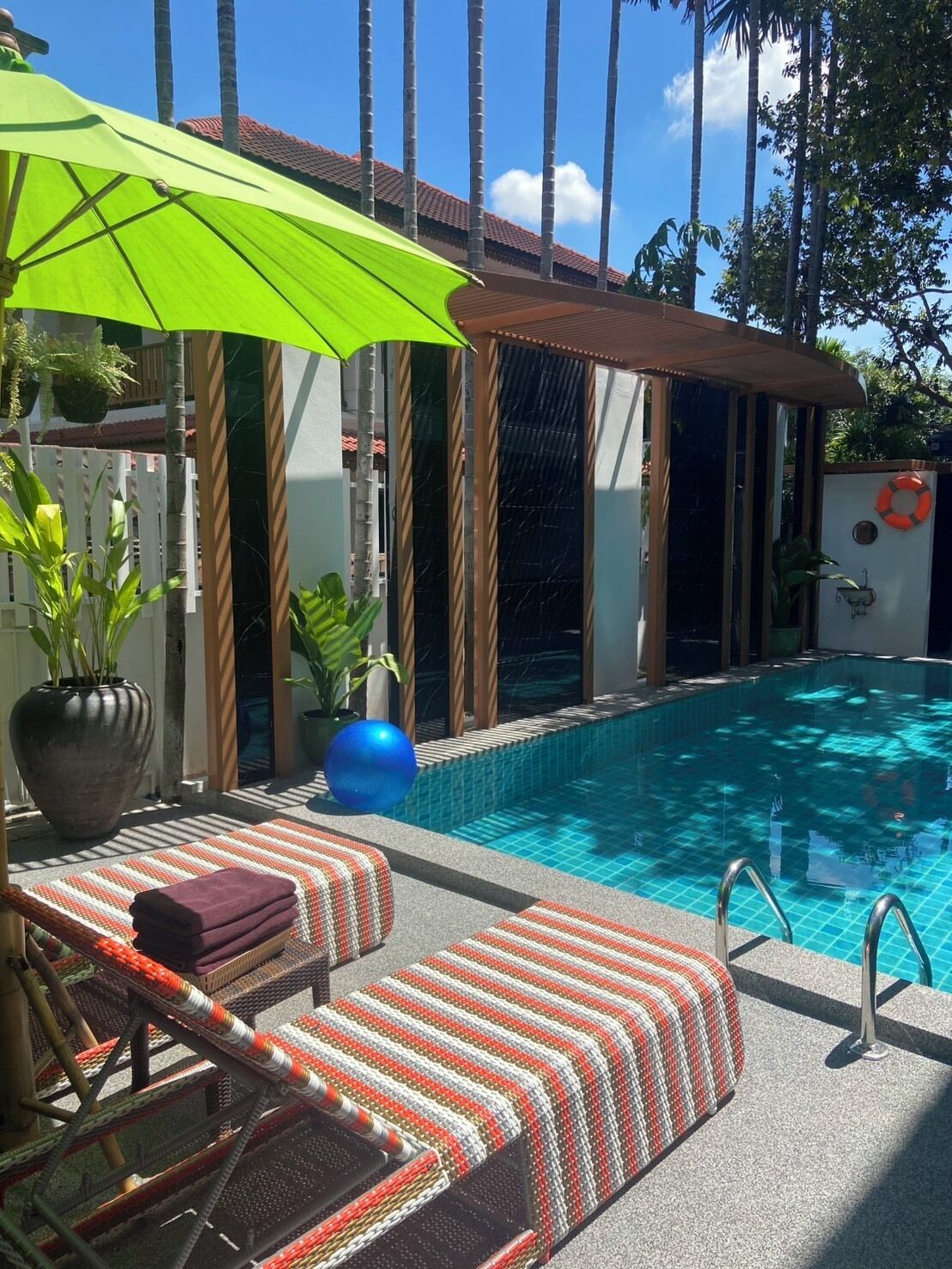 Piscina com espreguiçadeiras e um guarda-sol verde.