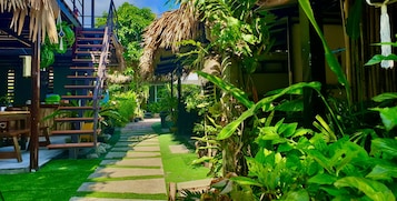 Uma trilha em um jardim tropical que leva a uma estrutura de madeira com telhado de palha.