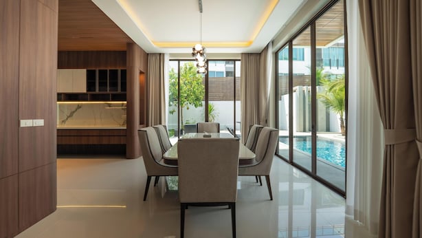 Uma área de jantar moderna com uma mesa e cadeiras de vidro, uma cozinha com armários de madeira e vista para uma piscina.