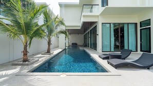 Uma área de piscina moderna com piscina transparente, espreguiçadeiras e uma palmeira.