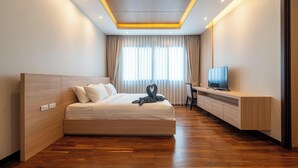 Quarto de hotel moderno com cama de madeira, escrivaninha com televisão de tela plana e uma janela grande com cortinas.