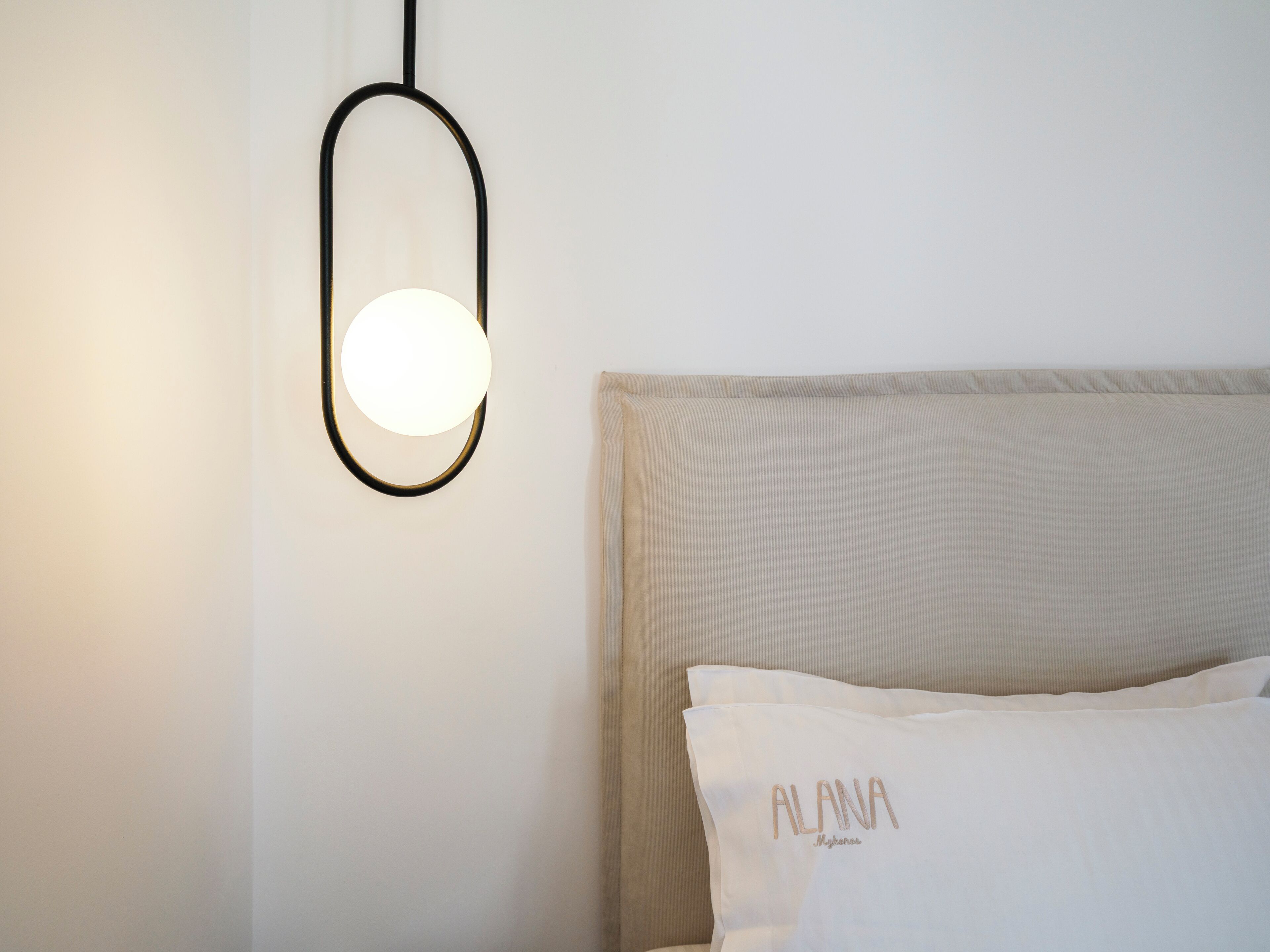 Uma cama com cabeceira bege e almofada bordada com o nome "ALANA".