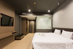 Quarto de hotel moderno com uma cama grande, televisão de tela plana na parede, ar condicionado embutido e porta deslizante para um banheiro.