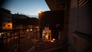 Uma varanda com grade, uma mesa com lanterna, velas e um vaso com flores.