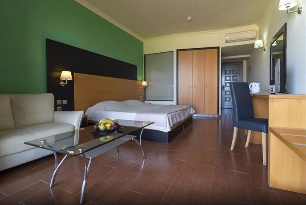 Quarto de hotel com uma cama, uma mesa de centro de vidro, um sofá, uma escrivaninha com cadeira e um guarda-roupa.