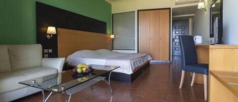 Quarto de hotel com uma cama, uma mesa de centro de vidro, um sofá, uma escrivaninha com cadeira e um guarda-roupa.