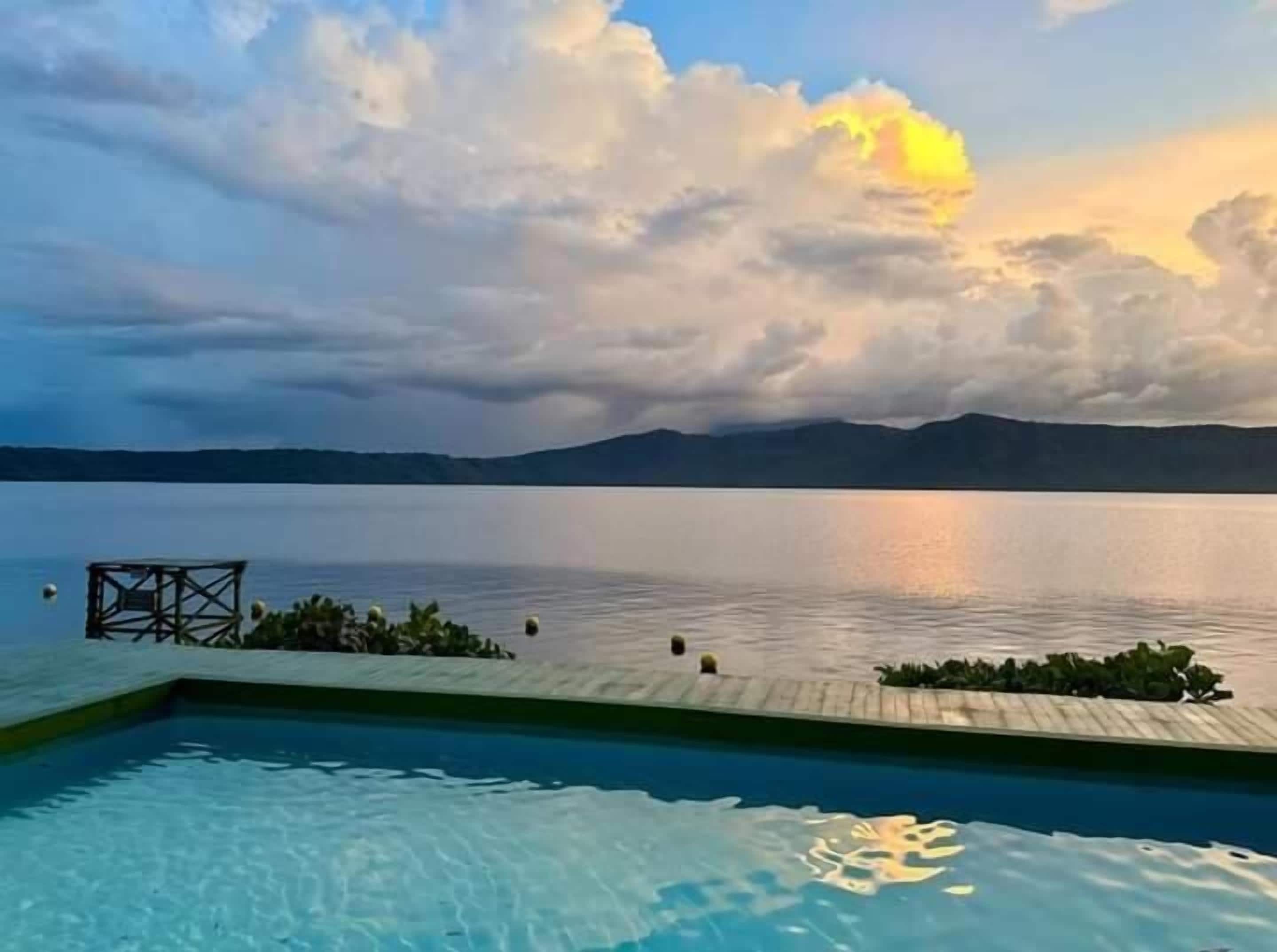 Piscina com vista para um lago tranquilo e montanhas ao longe.