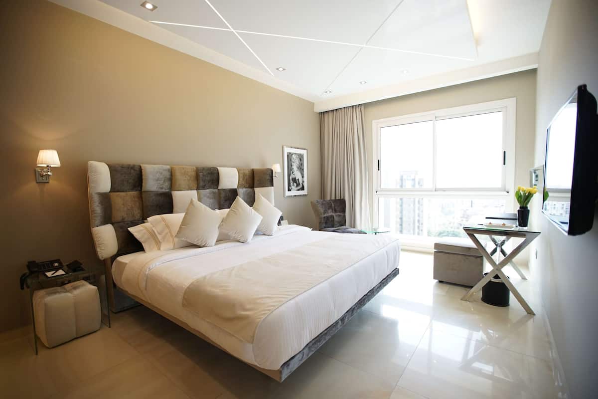 Quarto de hotel moderno com uma cama grande, uma escrivaninha e vista para a cidade pela janela.
