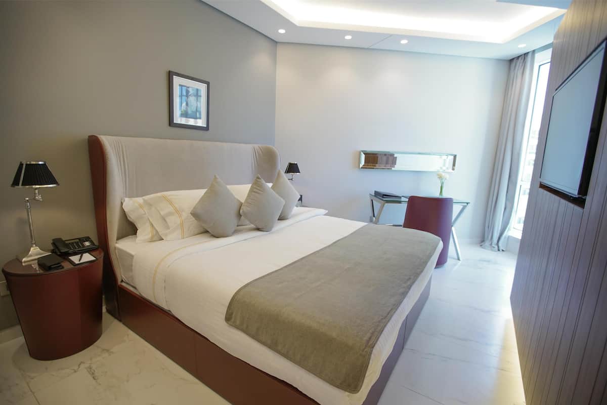 Quarto de hotel moderno com uma cama grande, luminárias de cabeceira, uma pequena mesa e uma televisão.