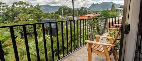 Varanda com chão de pedra, mobiliário de madeira e vista para um jardim exuberante e montanhas.