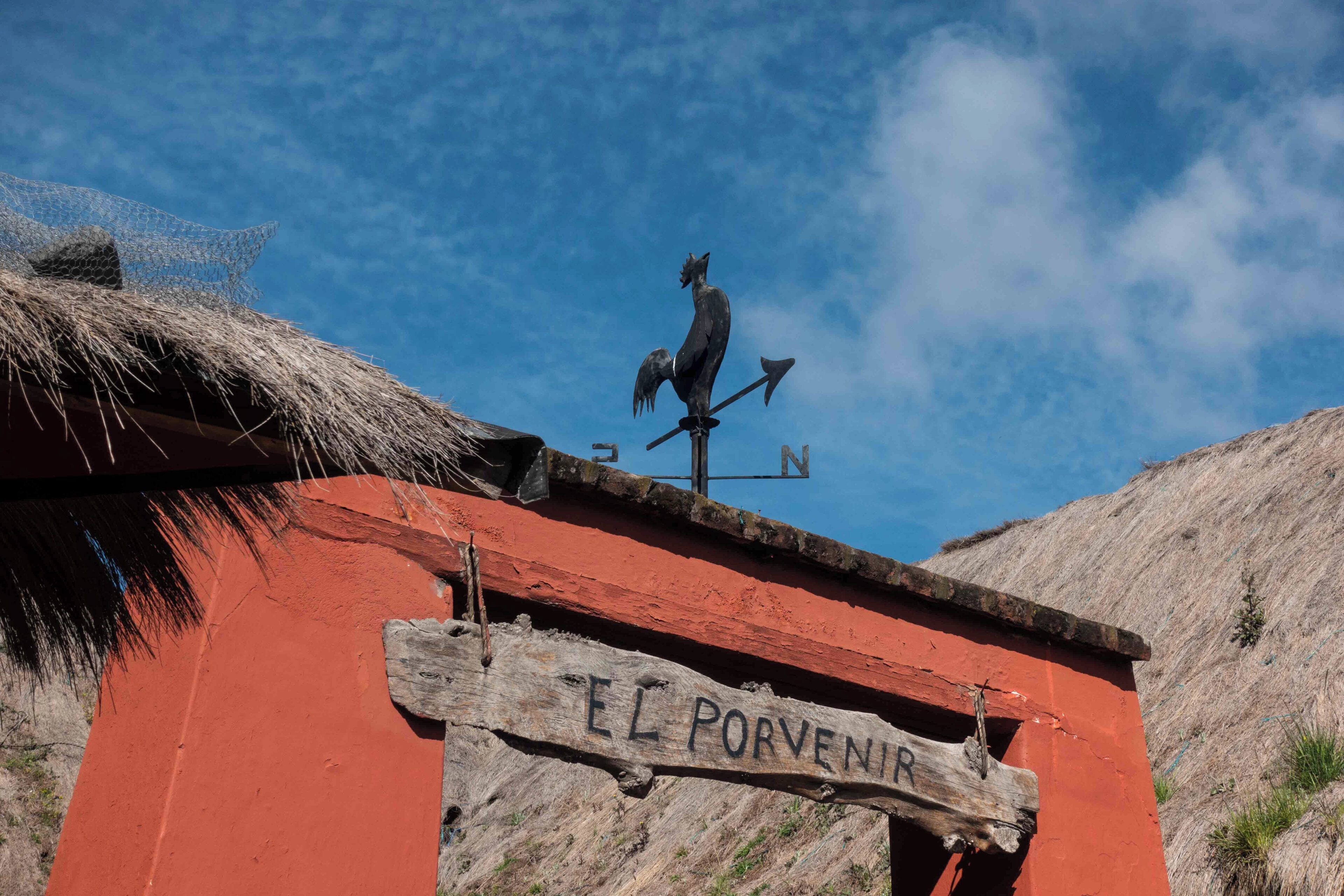 Uma girafa de vento em um edifício com uma placa de madeira que diz 'EL PORVENIR'.