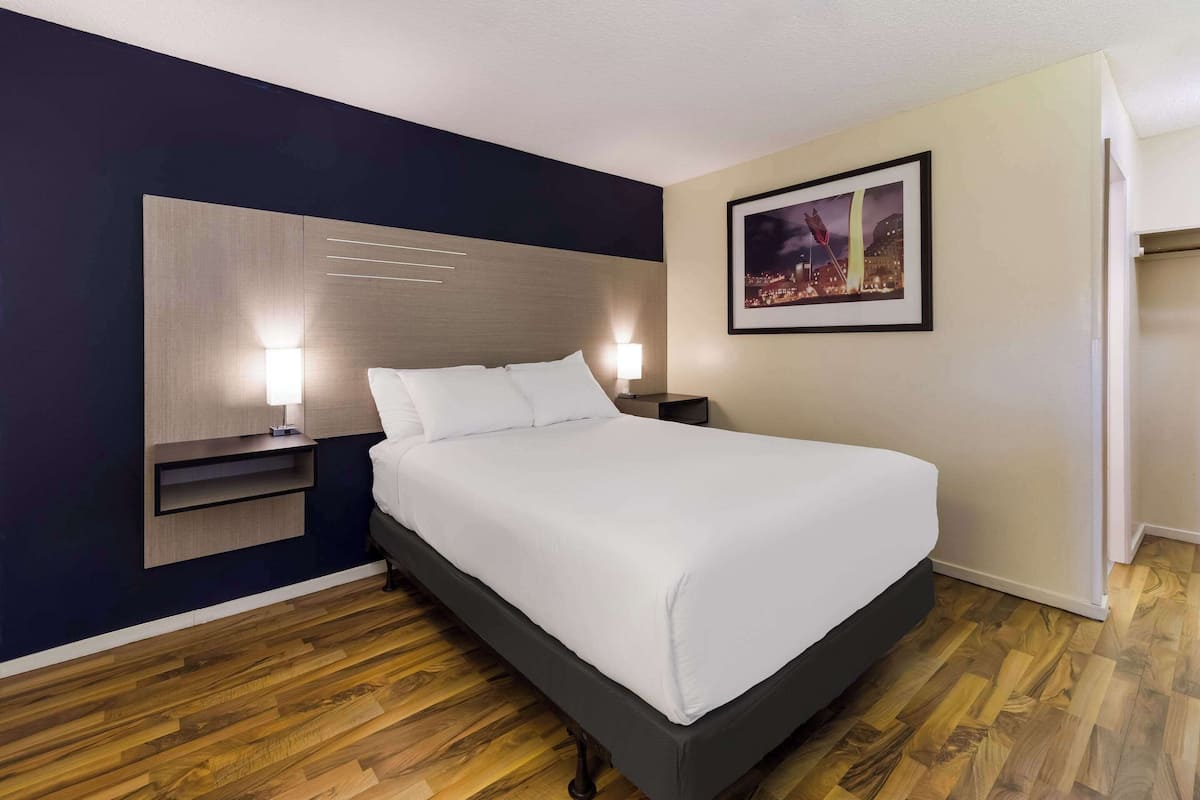 Quarto de hotel moderno com uma cama grande, mesas de cabeceira, televisão na parede e um quadro emoldurado.